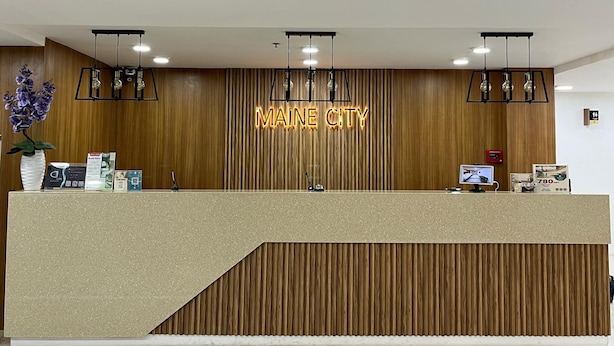 Uma receção com um painel de parede em madeira, um letreiro de néon com a inscrição "MAINE CITY" e uma planta em vaso.