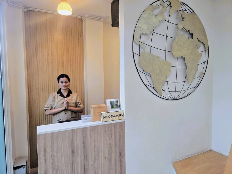 Balcão de recepção de hotel com um aviso de 'NÃO FUMAR', um globo decorativo e um painel de parede de madeira.