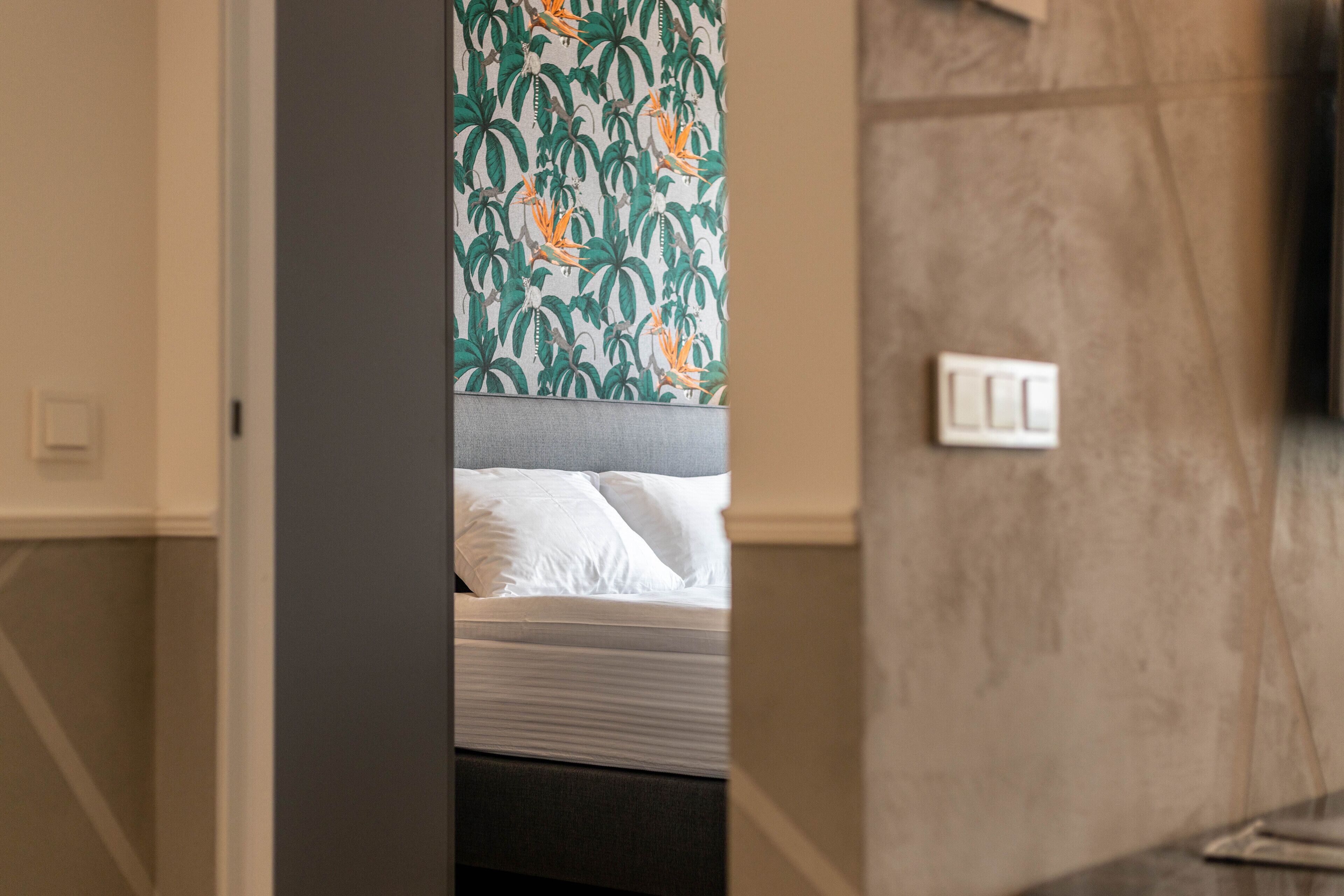 Quarto de hotel com uma cama, parede com padrão de folha tropical e um interruptor de luz.