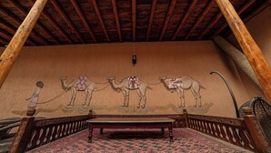 Um quarto com teto de madeira, um banco e uma parede com mural de camelo e cavalo.