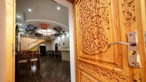 Uma porta de madeira com esculturas detalhadas, uma escadaria que leva a um segundo andar e uma área de jantar com mobiliário de madeira.