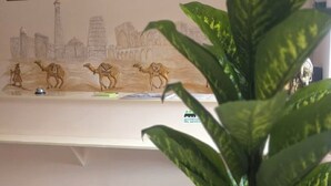 Uma mesa de recepção com relógios exibindo diferentes cidades, um mural com vista para a cidade e uma planta em vaso.