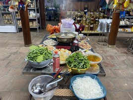 Uma mesa com diversos alimentos, incluindo vegetais, macarrão e uma panela em um fogão portátil.