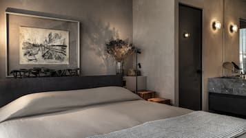 Quarto moderno com uma cama grande, uma obra de arte emoldurada, um vaso com flores secas, e um banheiro minimalista com espelho e pia.