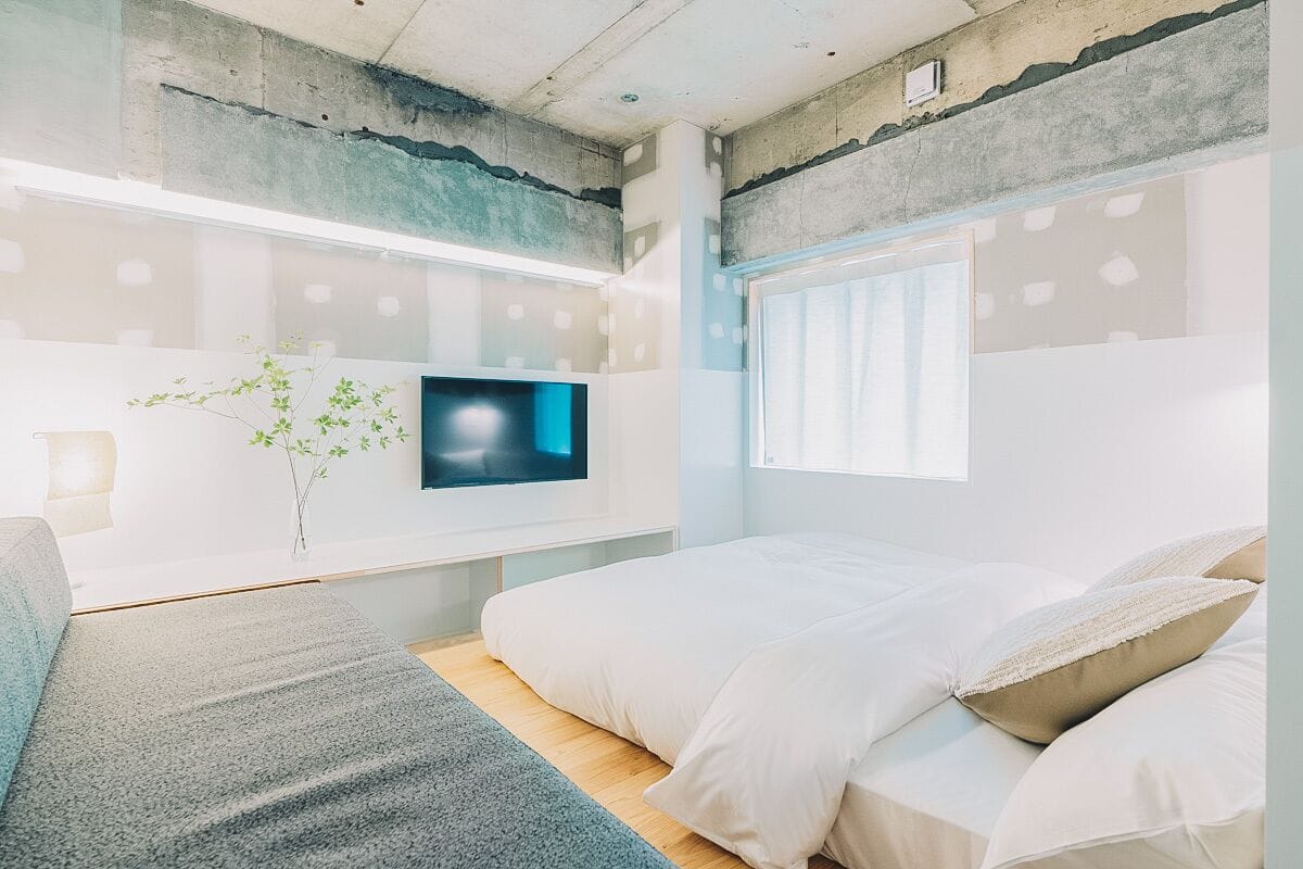 Um quarto moderno com uma cama, uma TV fixada na parede e uma janela.