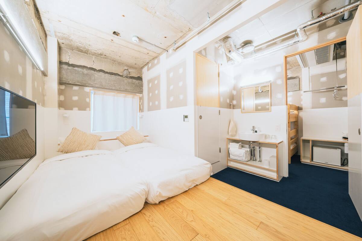 Quarto de hotel moderno com uma cama grande, roupeiro embutido, banheiro com espelho e pia, e uma televisão no lado esquerdo.