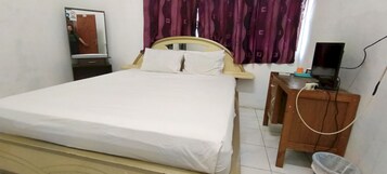 Quarto de hotel com cama, escrivaninha, cadeira, televisão e lixeira.