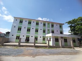 Um edifício com vários andares, fachada verde e branca, entrada com portão e acesso por um caminho de cascalho.