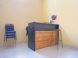 Um balcão de atendimento com painel de madeira e painel escuro, uma cadeira de metal e um banquinho de metal.