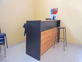 Uma mesa de recepção com acabamento preto e madeira, uma cadeira azul e um banquinho.