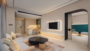 Uma sala de estar moderna com um sofá, duas mesas redondas, uma TV fixada na parede e uma área de piscina visível através de um arco.