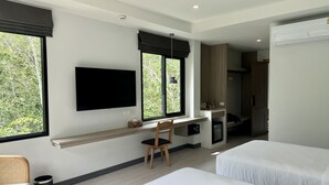 Quarto de hotel com duas camas, uma escrivaninha com cadeira, televisão na parede e janela com vista para árvores.