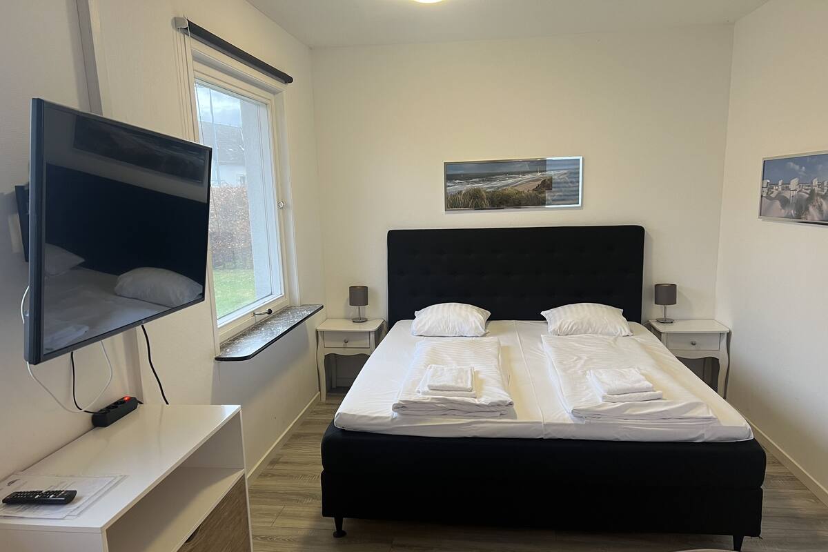Quarto de hotel com uma cama grande, uma televisão de tela plana na parede, uma janela com vista para o exterior e um quadro na parede.