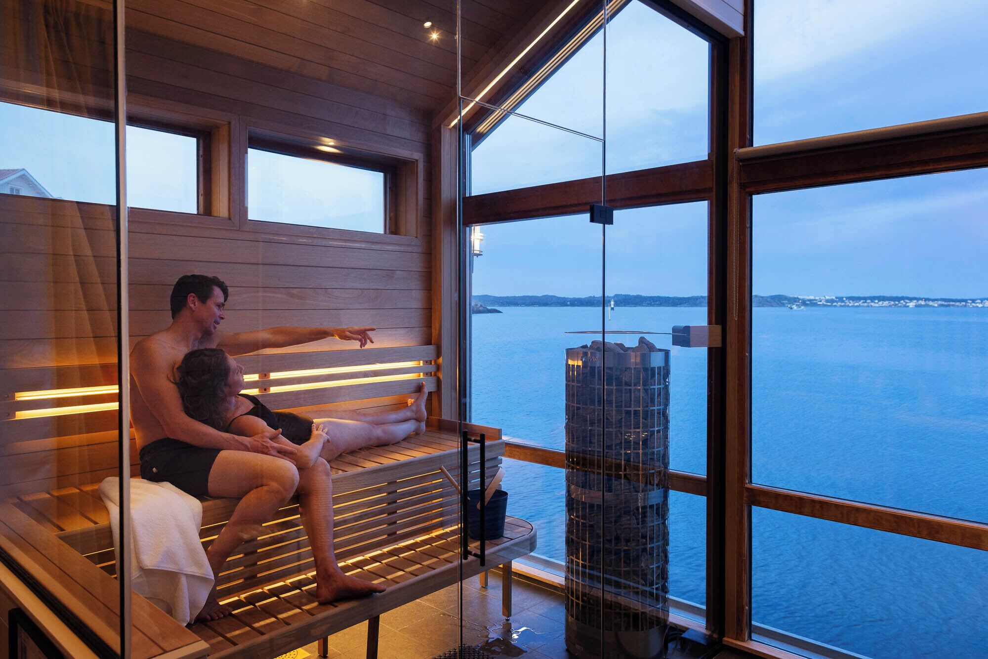 Uma sauna com vista para o mar, bancos de madeira e estrutura de vidro.