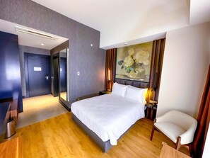 Quarto de hotel moderno com uma cama grande, uma escrivaninha, uma cadeira e um quadro na parede.