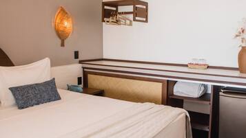 Quarto de hotel com uma cama grande, uma mesinha de cabeceira, ar-condicionado fixado na parede e uma luminária decorativa.