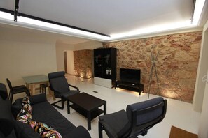 Uma sala de estar moderna com sofá, poltronas, mesa de centro, televisão e parede de pedra.