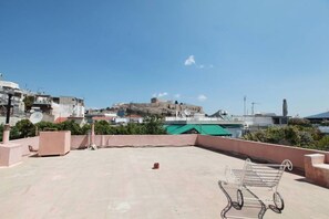 Terraço no telhado com uma cadeira de metal, uma pequena lixeira e vista de um edifício histórico ao fundo.
