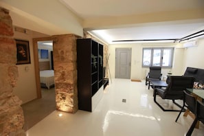 Uma sala de estar moderna com um pilar de pedra, um rack de entretenimento preto e uma área de jantar com cadeiras e uma mesa pretas.