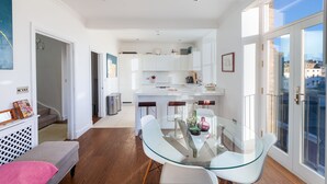 Uma cozinha moderna com armários brancos, uma ilha central e uma área de jantar com mesa e cadeiras de vidro.