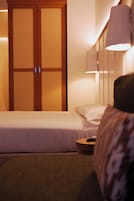 Quarto de hotel com cama, guarda-roupa de madeira e abajur.