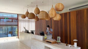 Uma área de recepção com um balcão de madeira, luminárias pendentes de vime e uma grande janela com vista para o exterior.