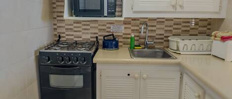 Uma cozinha compacta com fogão a gás, micro-ondas embutido, pia e uma pequena área de bancada.