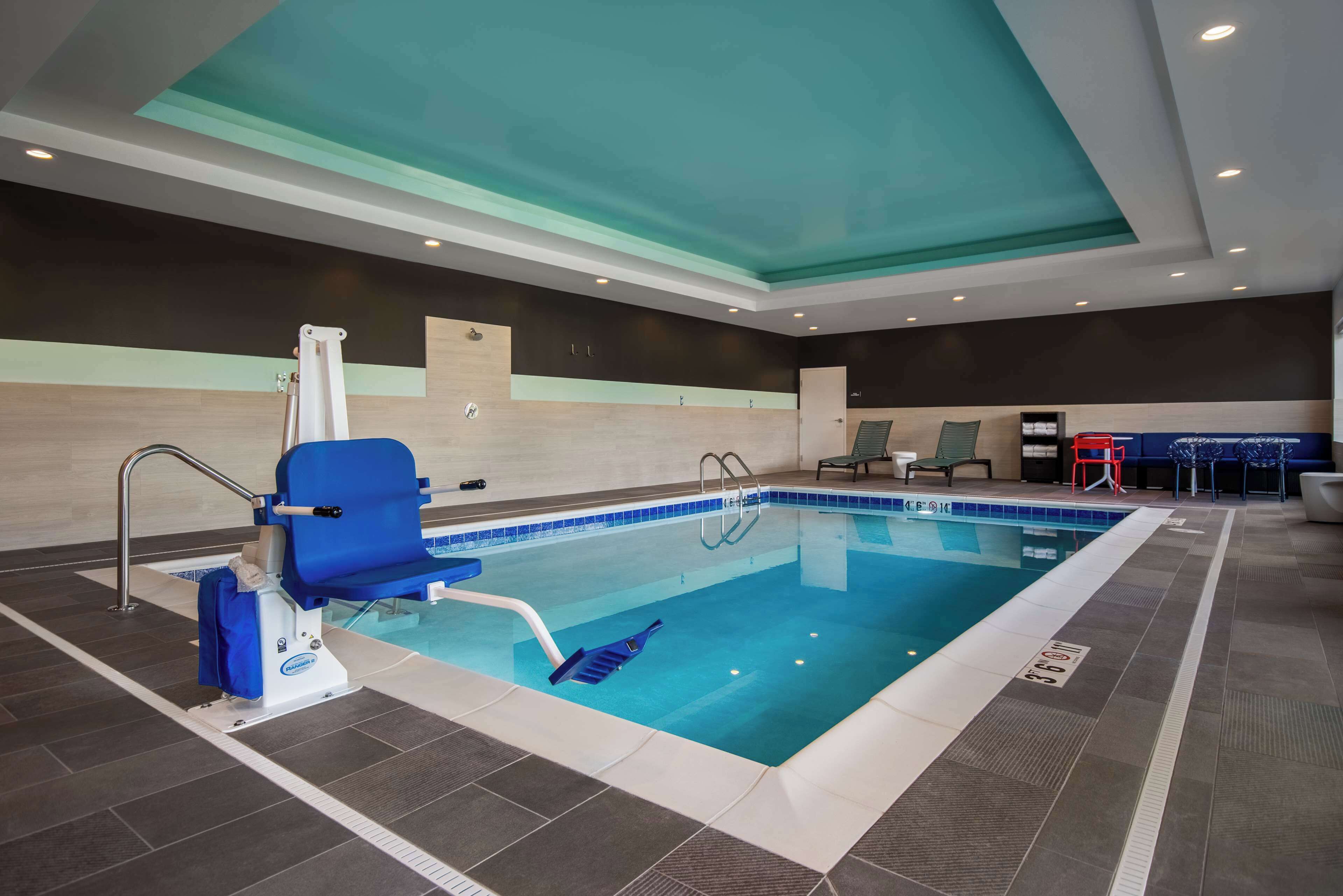 Piscina interna com cadeira azul, área de trocas para bebês e espaço de estar com cadeiras e mesa.