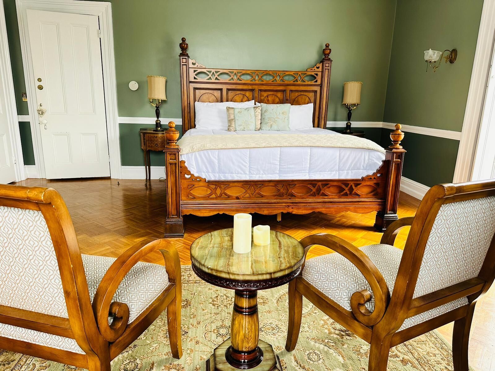 Quarto com cama de dossel de madeira, duas mesas de cabeceira e duas poltronas estofadas.
