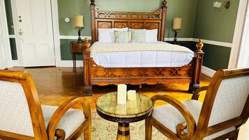 Quarto com cama de dossel de madeira, duas mesas de cabeceira e duas poltronas estofadas.