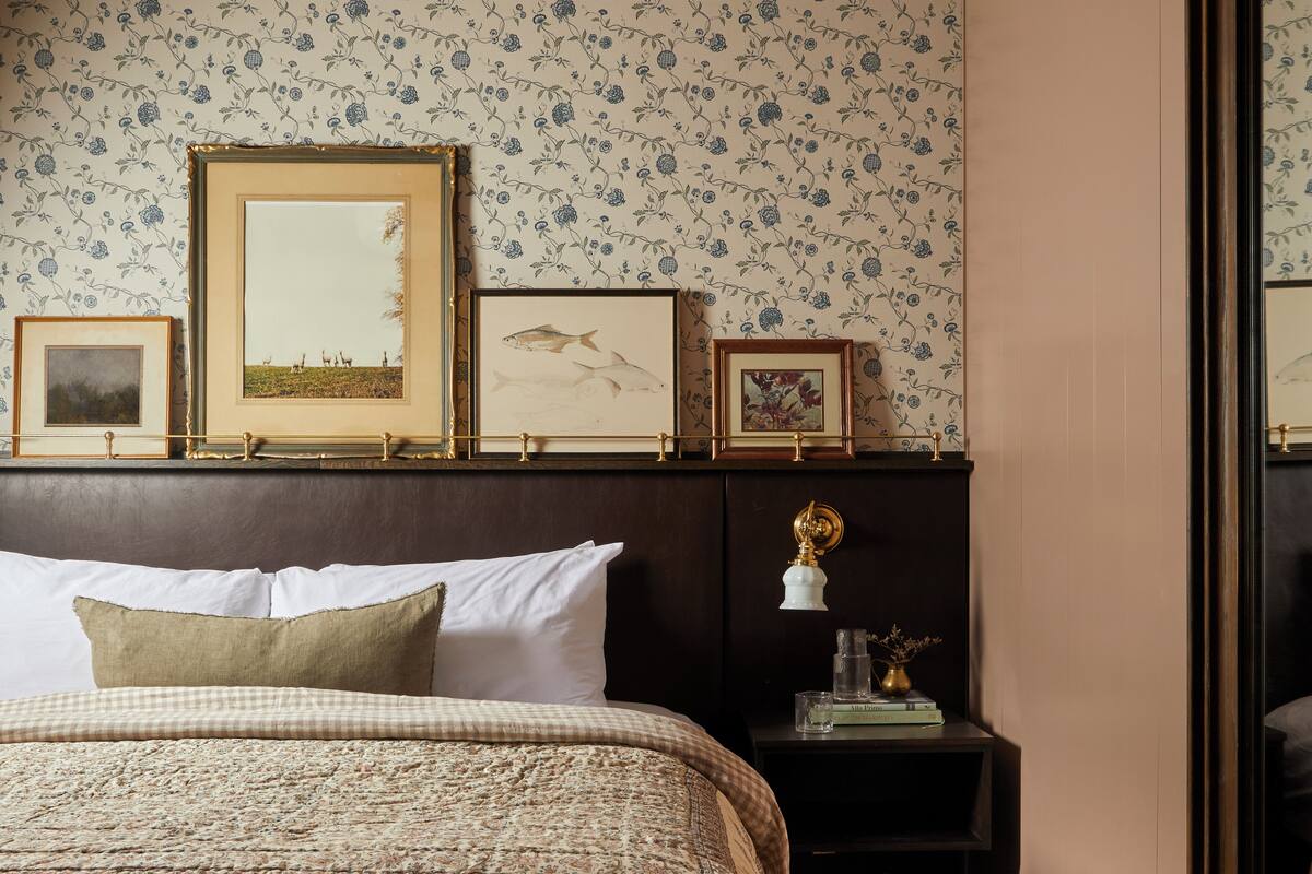 Quarto com cama, mesa de cabeceira e parede com quadros.