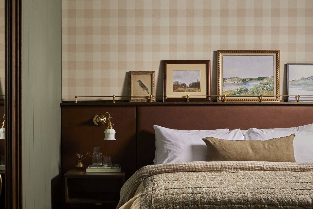 Quarto com parede xadrez, cama com roupa de cama estampada, mesa de cabeceira com abajur e quadros acima da cama.