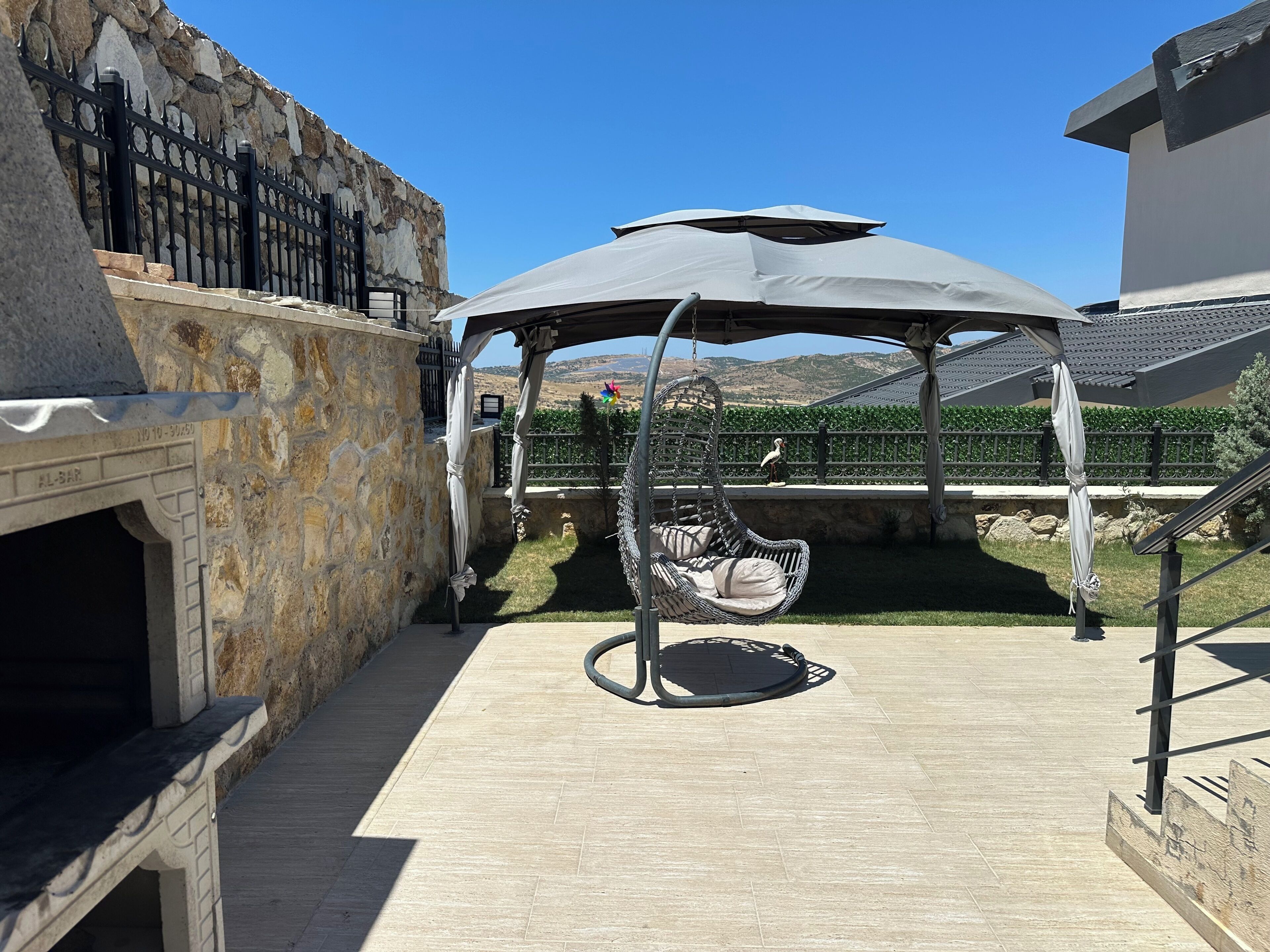 Uma área de pátio com uma cadeira suspensa, um espaço de estar coberto e um muro de pedra.
