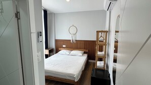 Um quarto com uma cama de madeira, uma mesa de cabeceira, um criado-mudo e um ar condicionado fixado na parede, além de uma decoração com um sonho-apanhador.