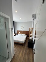 Um quarto com uma cama de madeira, uma mesa de cabeceira, um criado-mudo e um ar condicionado fixado na parede, além de uma decoração com um sonho-apanhador.