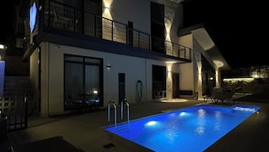 Uma casa moderna de dois andares com piscina, mobiliário de exterior e varanda.