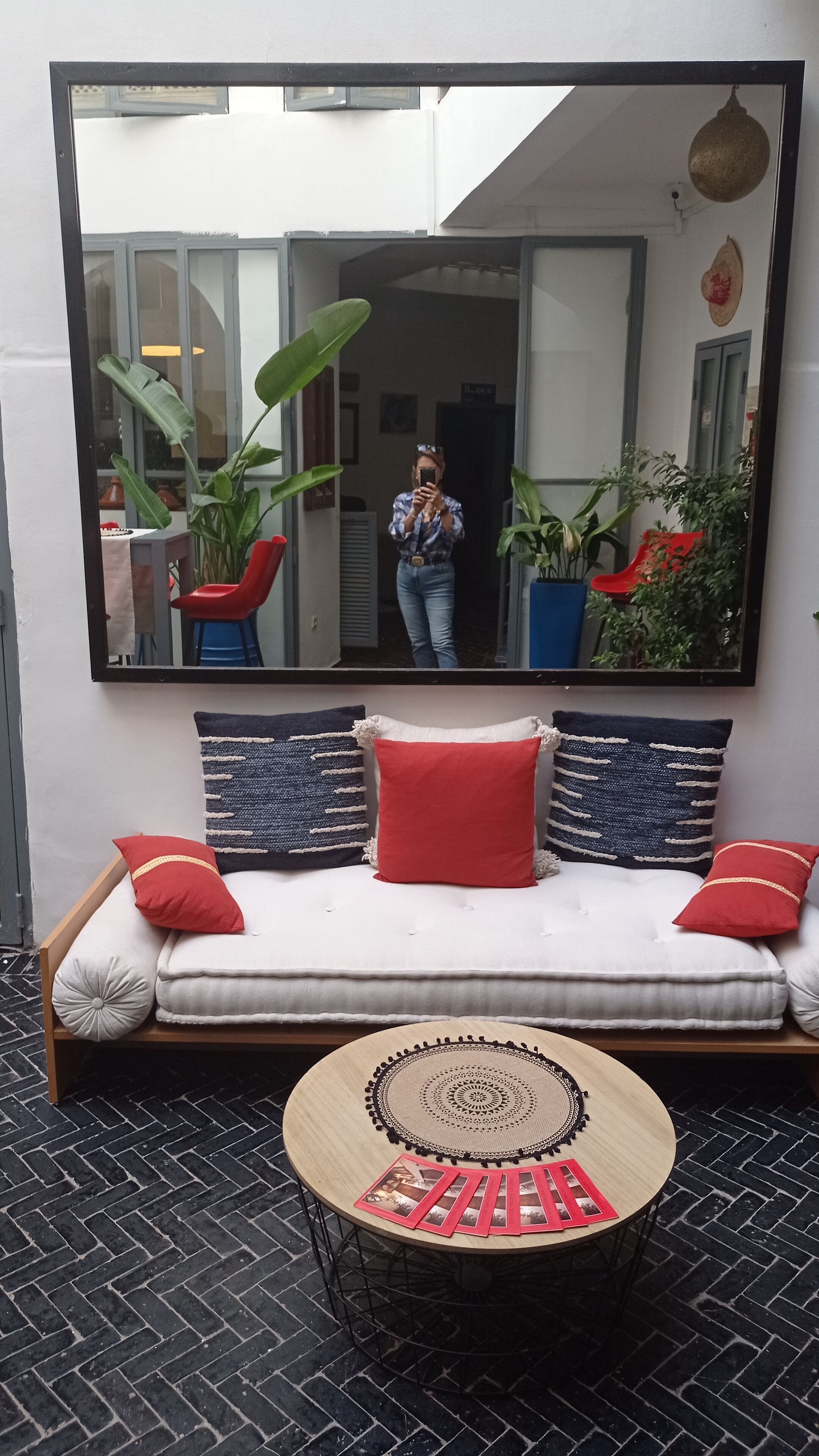 Uma sala de estar moderna com um espelho grande, um sofá com almofadas vermelhas e azuis e uma mesa de centro redonda com um apoio de tecido.