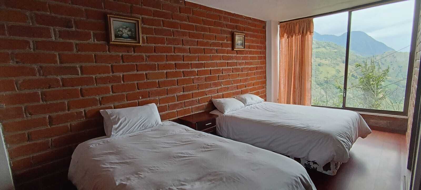 Quarto com duas camas, parede de tijolos e uma janela grande com vista para as montanhas.
