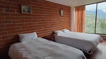 Quarto com duas camas, parede de tijolos e uma janela grande com vista para as montanhas.