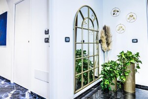 Um corredor com piso de mármore, janela de metal decorativa e plantas em vasos.