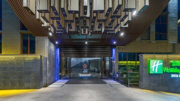 Entrada de hotel com design moderno, fachada de tijolos, acesso por vidro e uma placa com o nome do hotel.