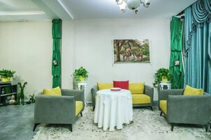 Uma sala de estar com dois sofás cinza, uma mesa redonda branca e cortinas verdes.