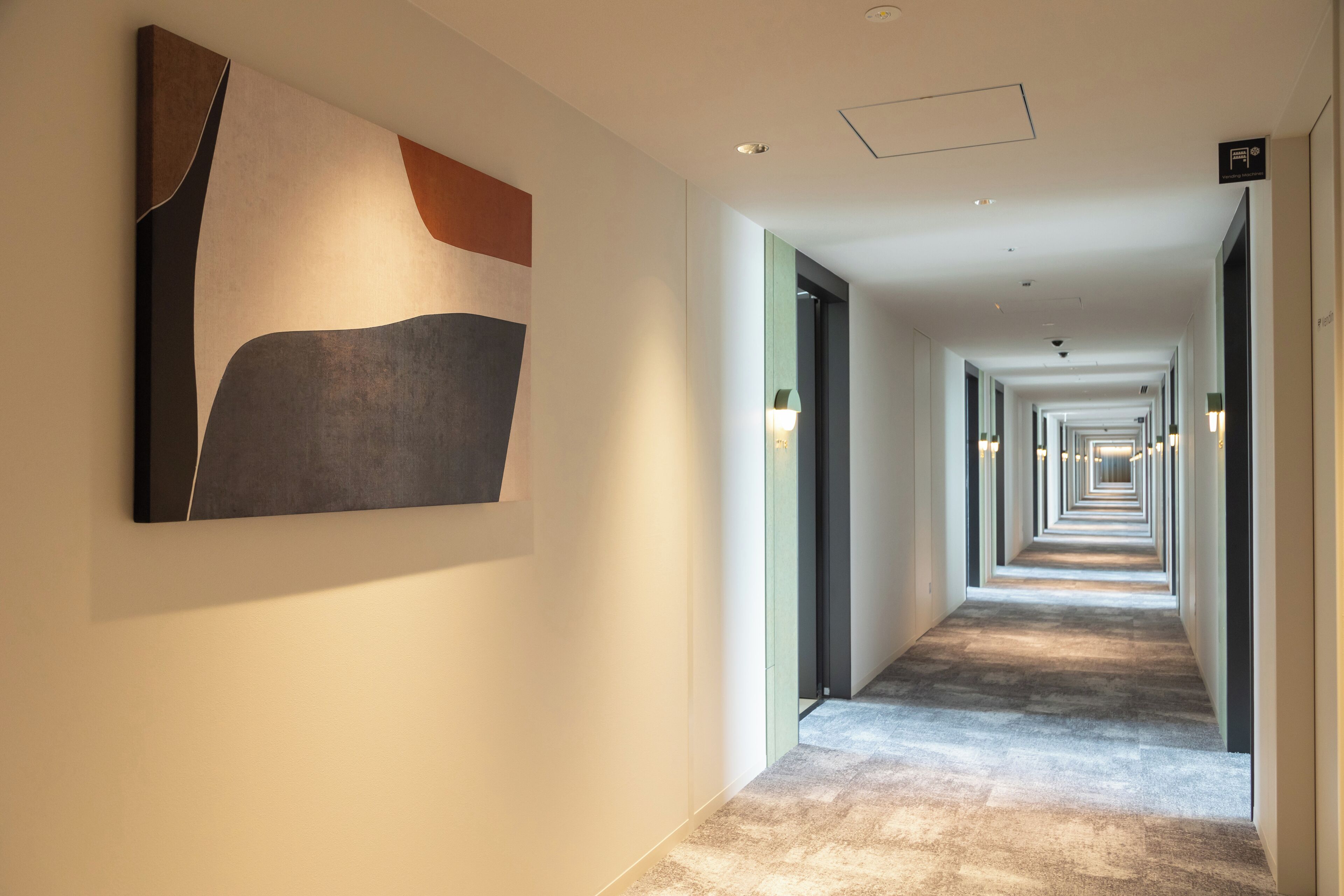 Um corredor com uma pintura abstrata moderna na parede, piso coberto de carpete e uma série de portas que levam a quartos.