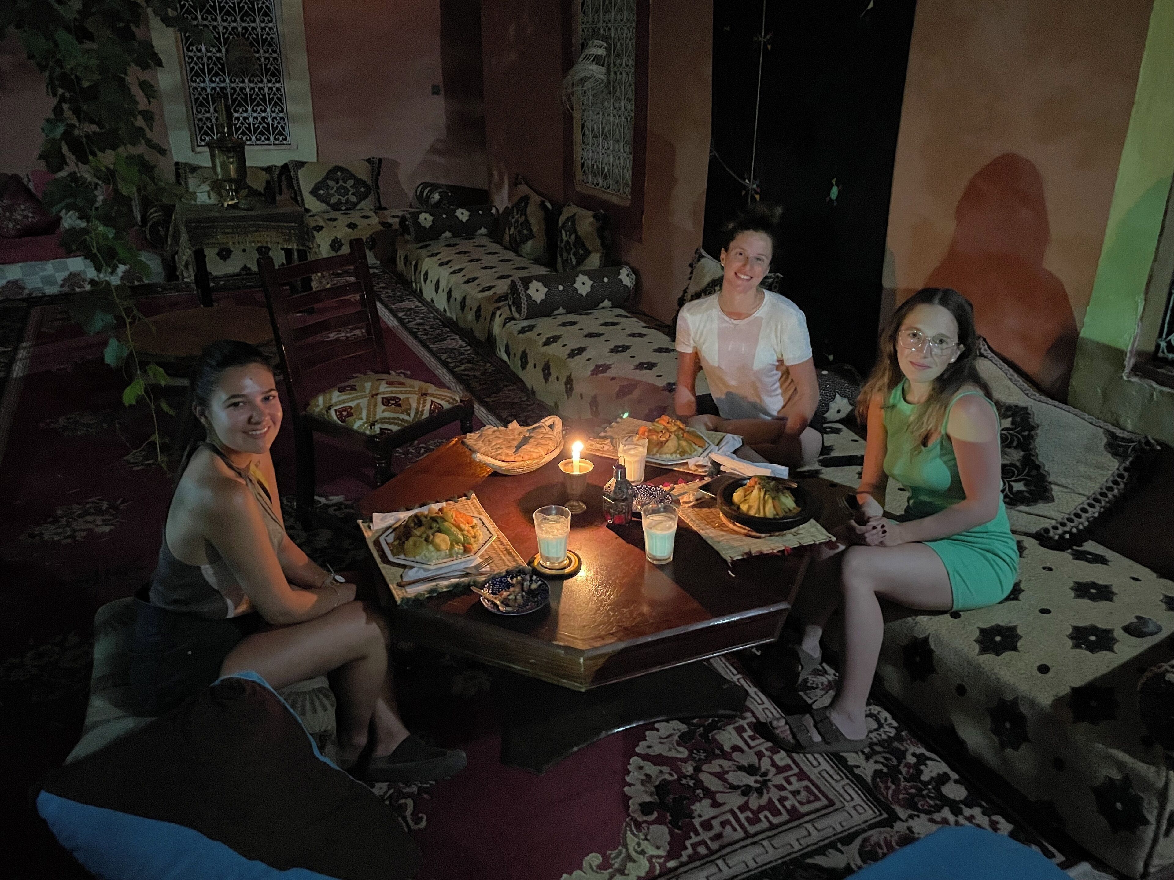 Uma sala de jantar com mesa posta para três pessoas, rodeada por sofás estampados e uma parede decorativa.