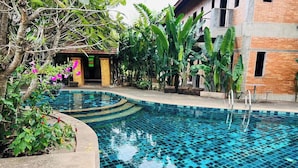 Piscina com borda revestida, rodeada por vegetação exuberante e um edifício com fachada de tijolos.