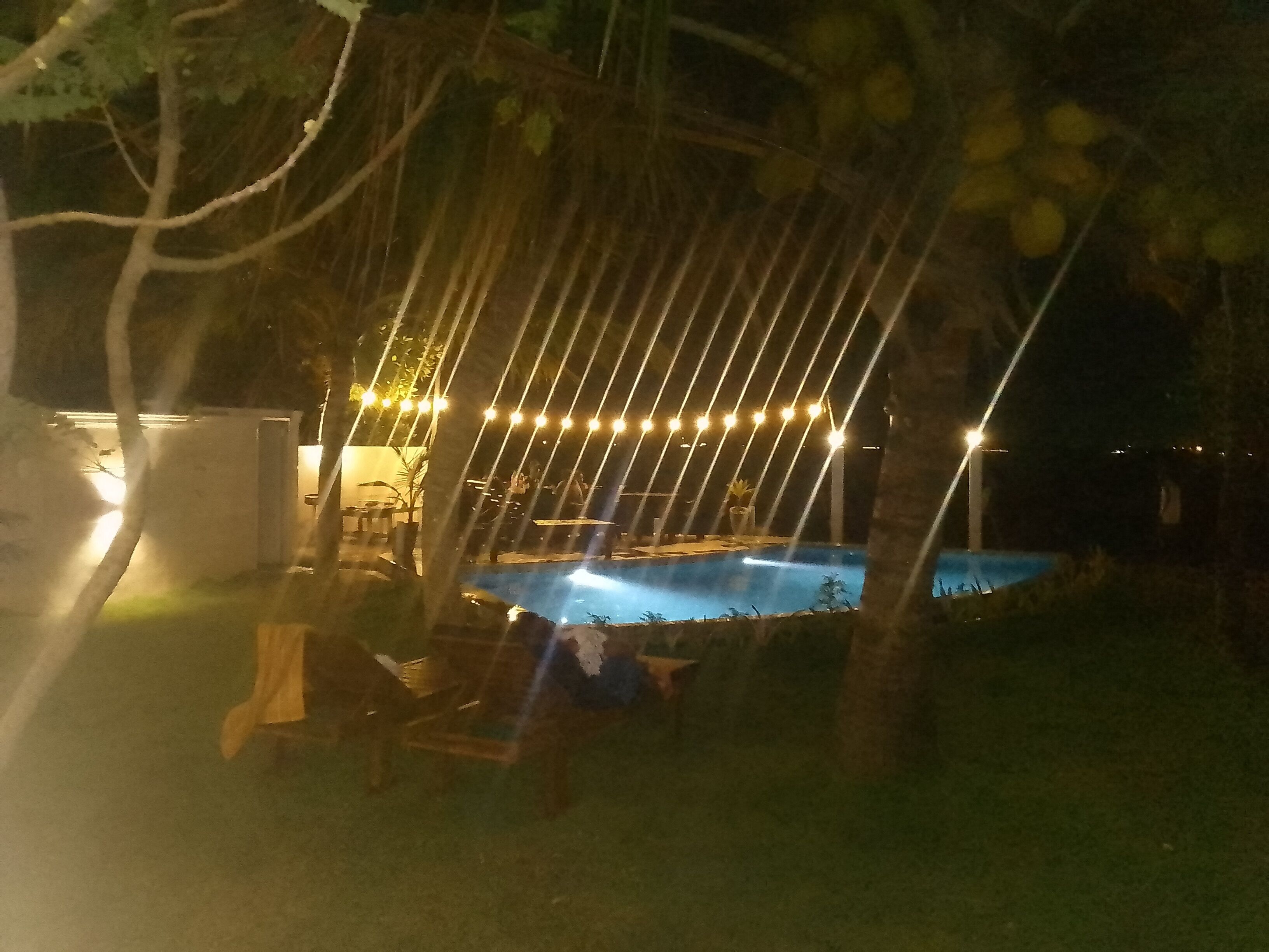 Uma rede estendida entre árvores em um quintal com piscina e área de estar externa.