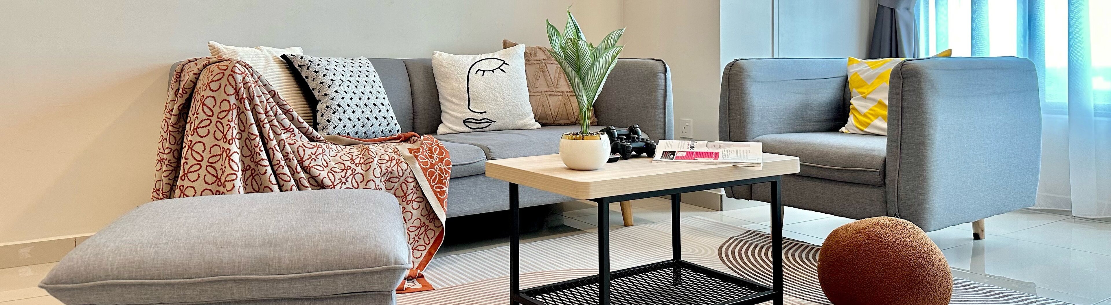 Uma sala de estar moderna com sofás cinzas, uma mesa de centro e um cobertor estampado.