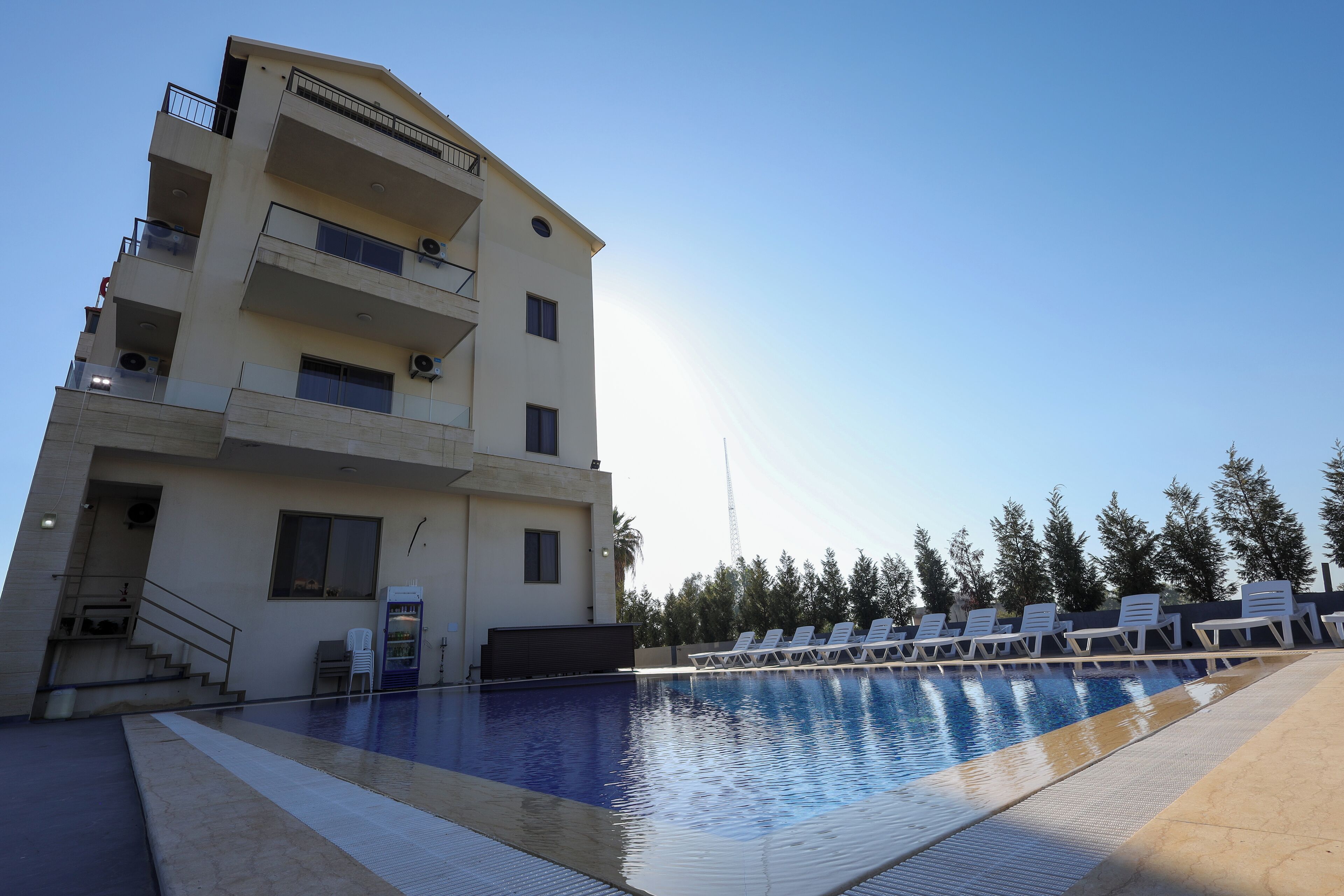 Área de piscina com espreguiçadeiras e um edifício com várias varandas.
