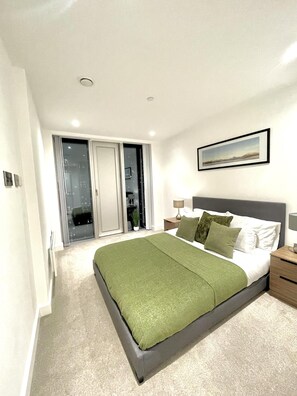 Quarto moderno com uma cama grande, mesa de cabeceira, abajur e porta de vidro deslizante para uma varanda.