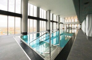 Piscina interior com paredes de vidro transparente, grandes janelas e design moderno.
